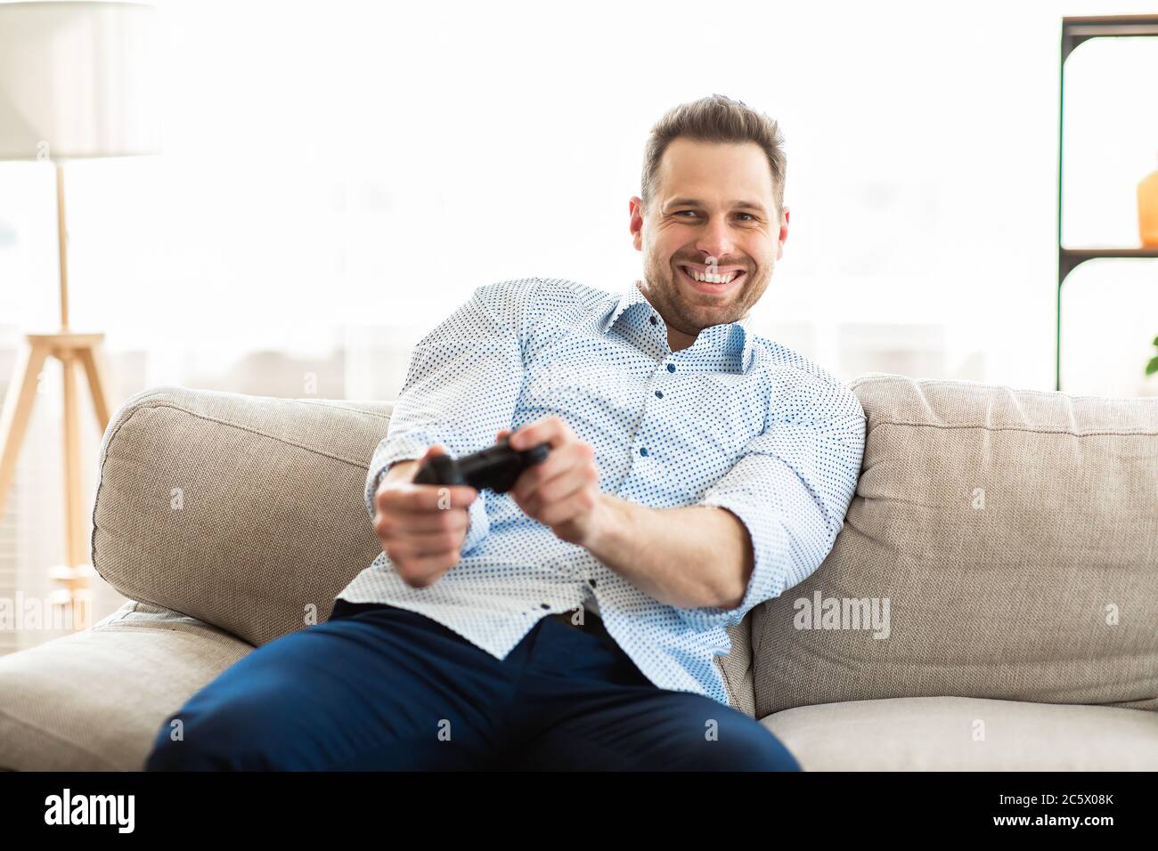 Young man sitting on couch playing video games Stock Photo - Alamy