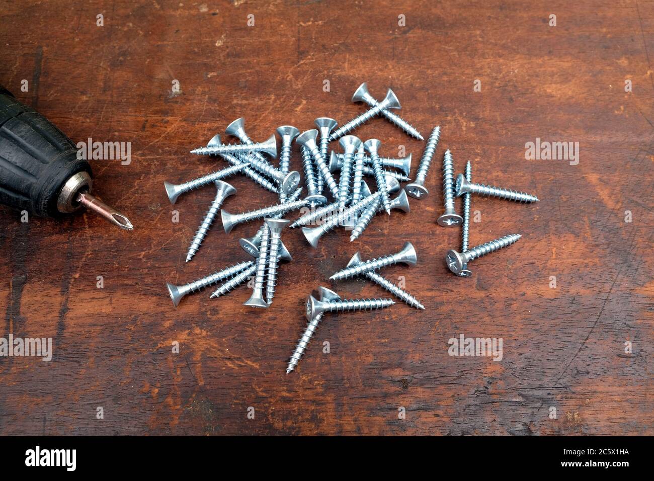 Heap of many light gray screws and old motor screw driver on brown ...