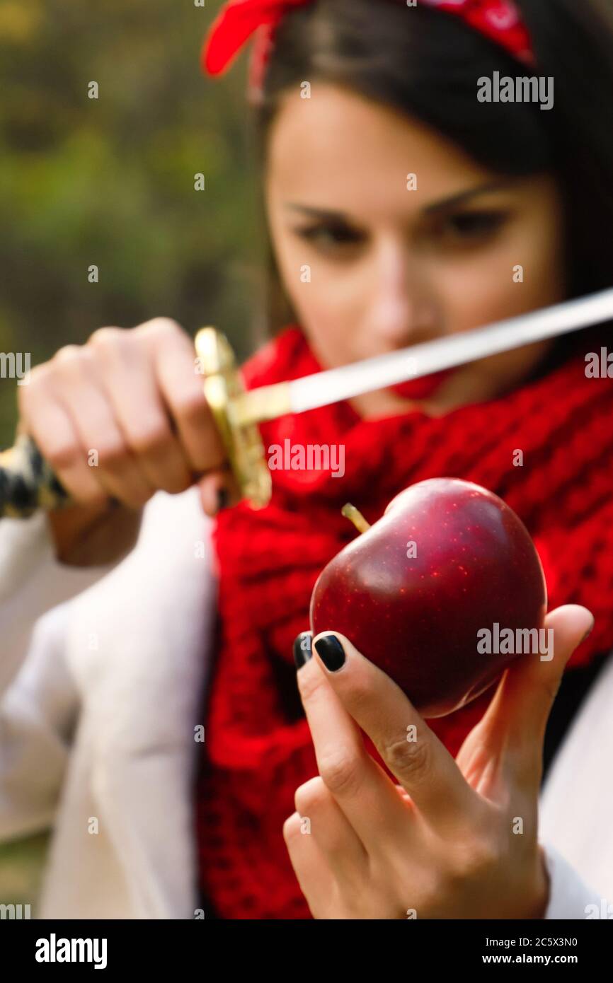 A woman with a sharp blade in her hands is about to cut a red apple ...