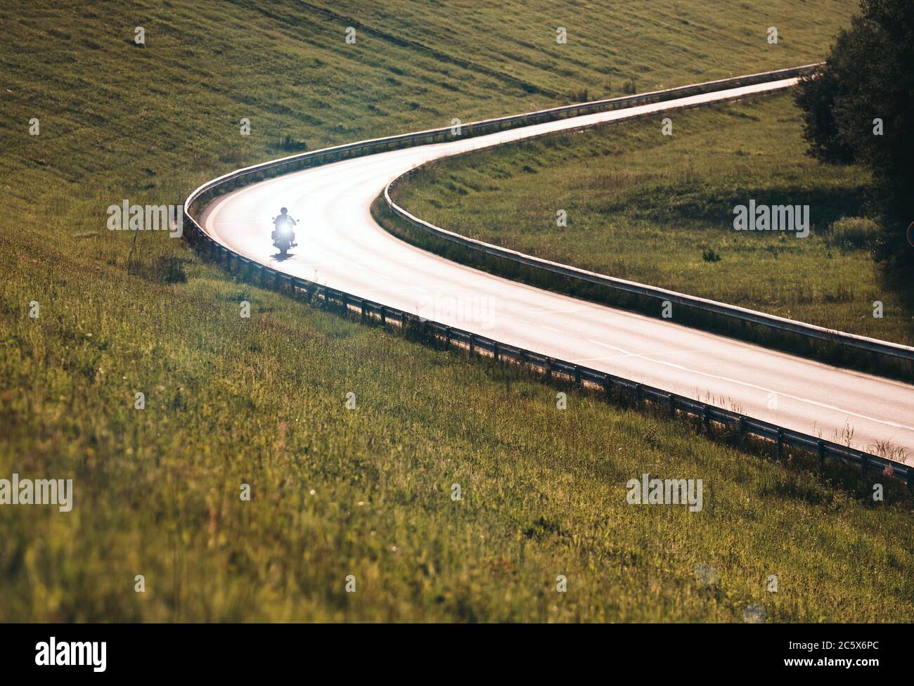 Motorcycle with headlight moving by the highway illuminated with back ...