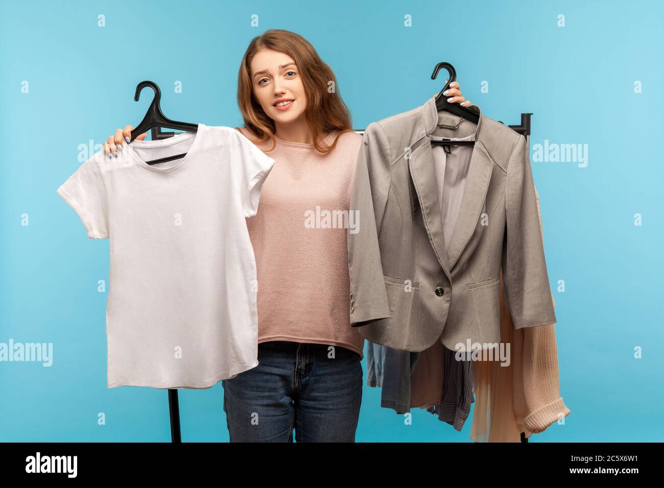 Uncertain confused woman shopper holding clothes on racks and looking ...