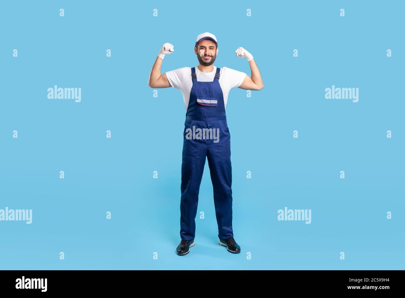 Full length cheerful handyman in overalls, cap and protective gloves ...