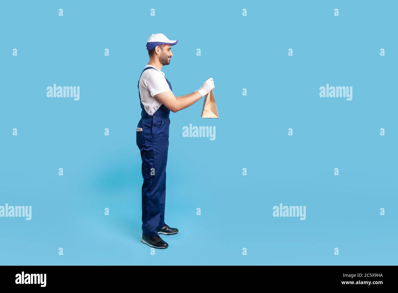 Side view, courier in blue uniform giving groceries bag and smiling ...