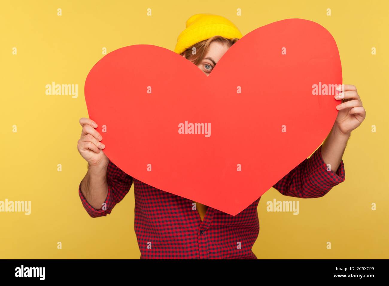 Modest guy hiding behind huge red paper heart, looking at camera ...