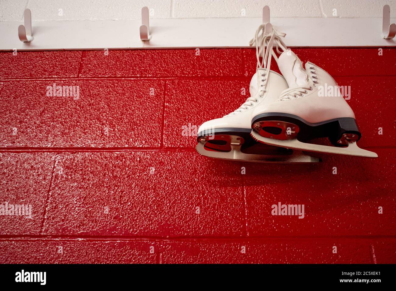 Bottom view of figure skates hanging over red wall in locker room with ...