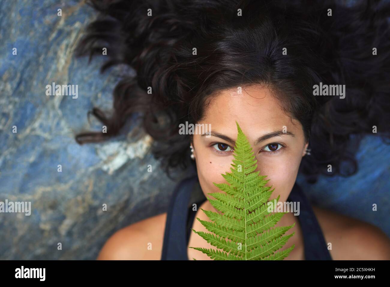 Woman with a fern on her face. She's lying on a rock and covers half ...
