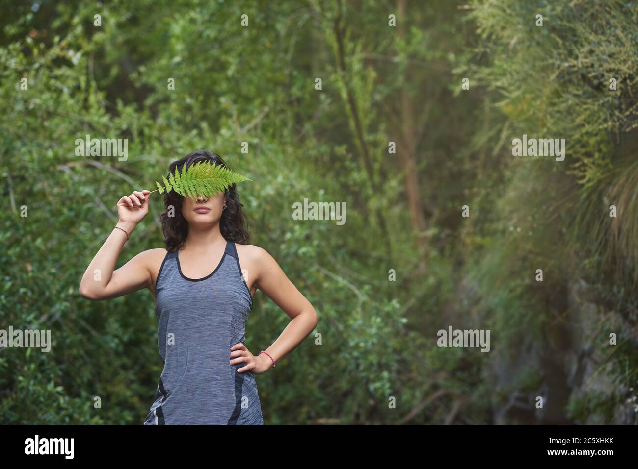 Woman with a fern on her face. She is in a river and covers half of her ...