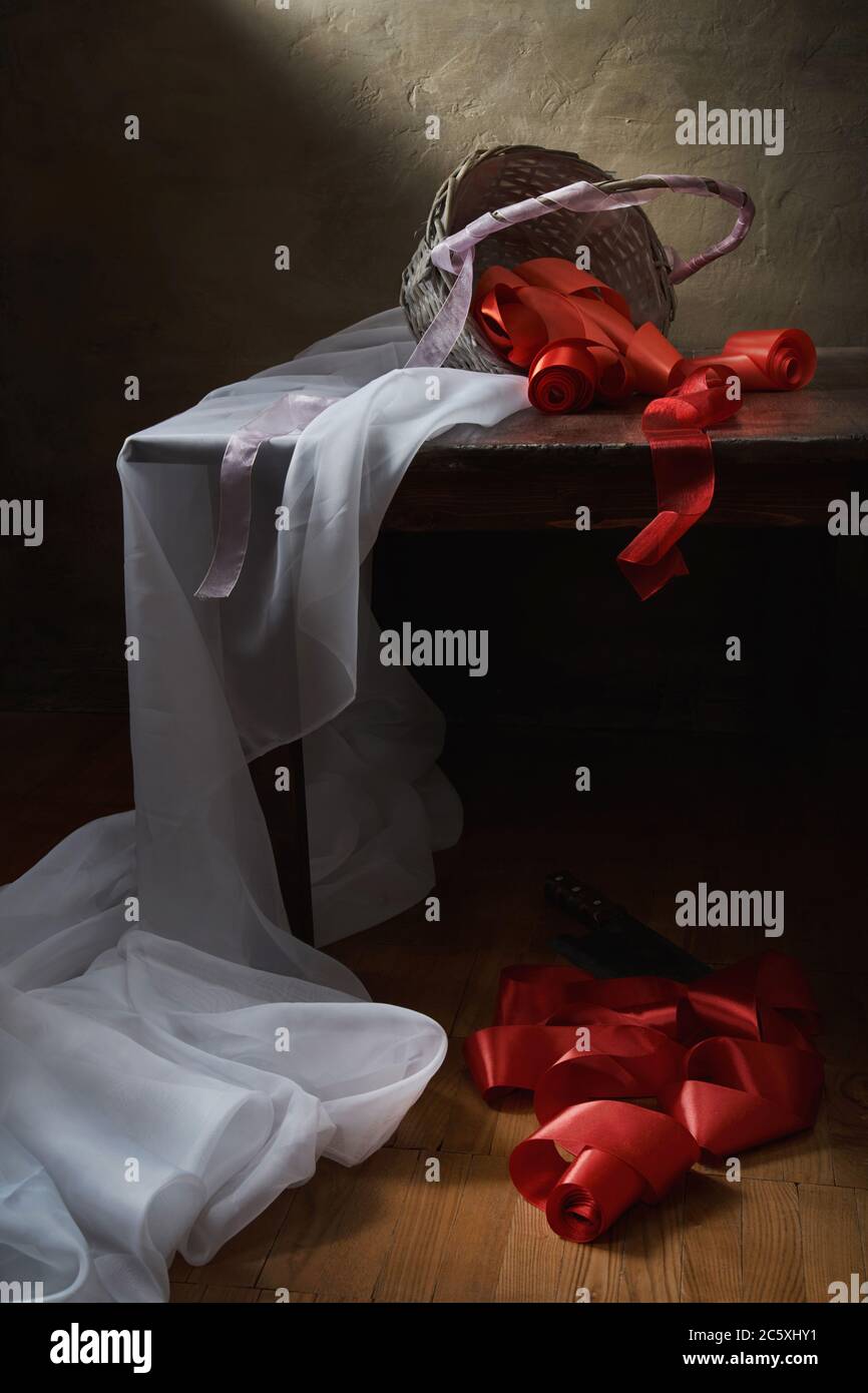 Still life with a white cloth and an overturned basket of red ribbons ...