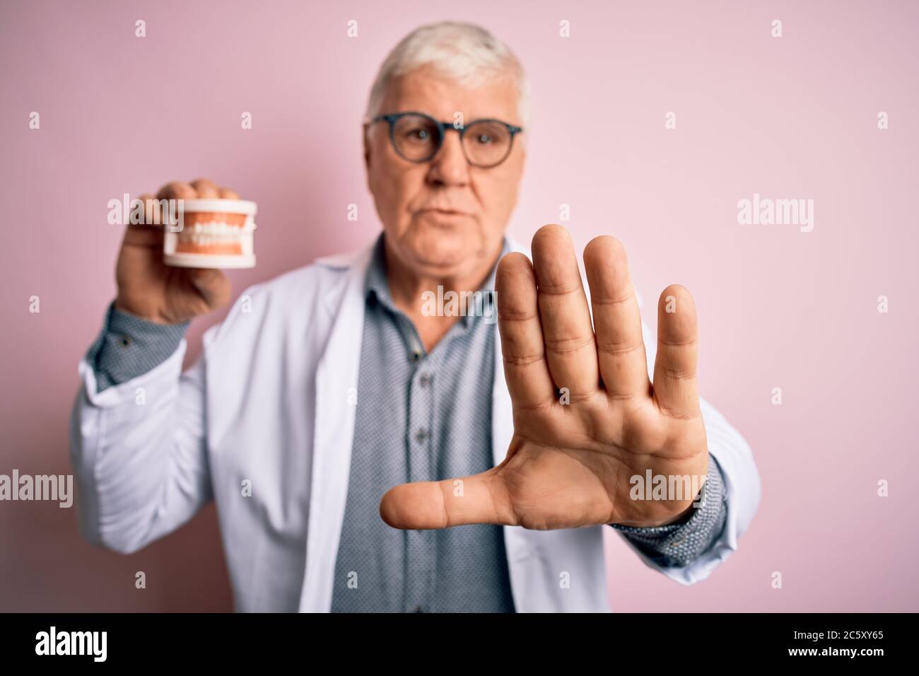 Senior handsome hoary dentist man wearing coat holding denture teeth ...