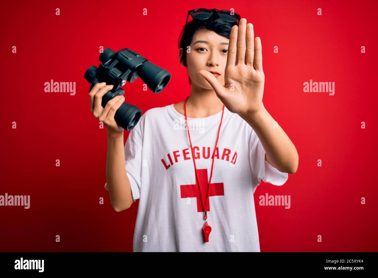 Young beautiful asian lifeguard girl using whistle and binoculars over ...