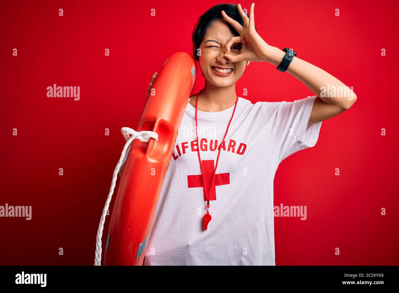 Young beautiful asian lifeguard girl using whistle holding orange float ...