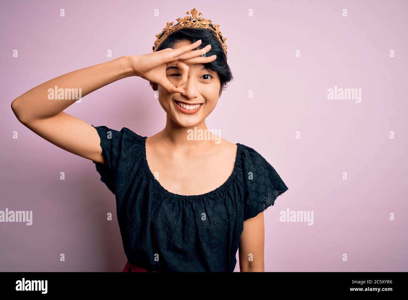 Young beautiful chinese woman wearing golden crown of king over ...
