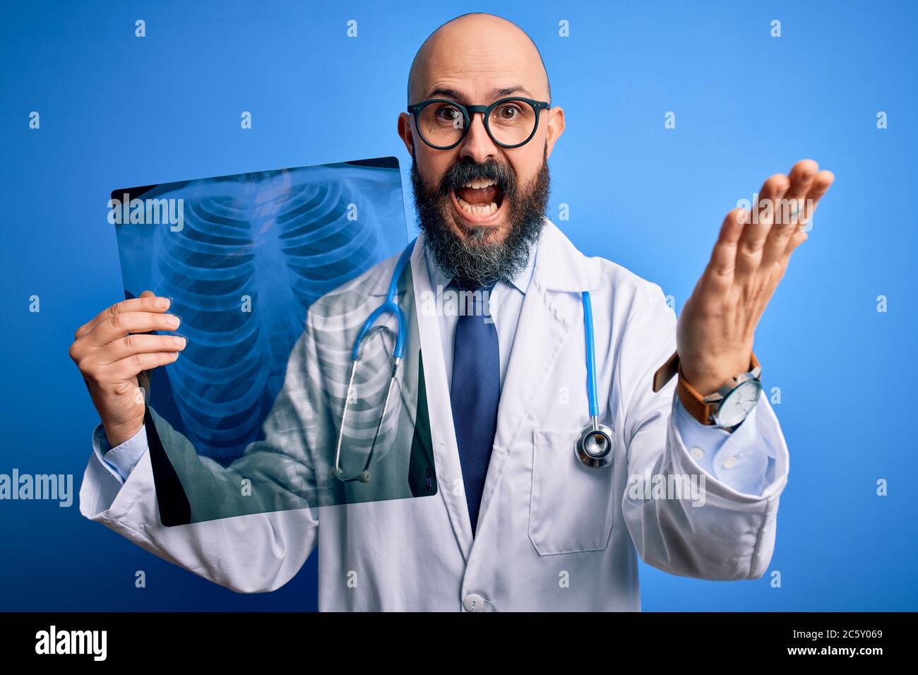 Handsome bald doctor man with beard wearing stethoscope holding chest ...