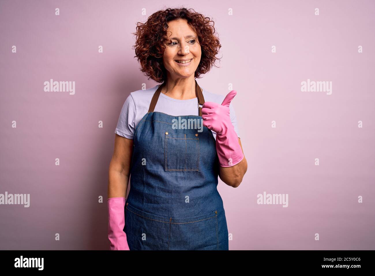 Middle age curly hair woman cleaning doing housework wearing apron and ...