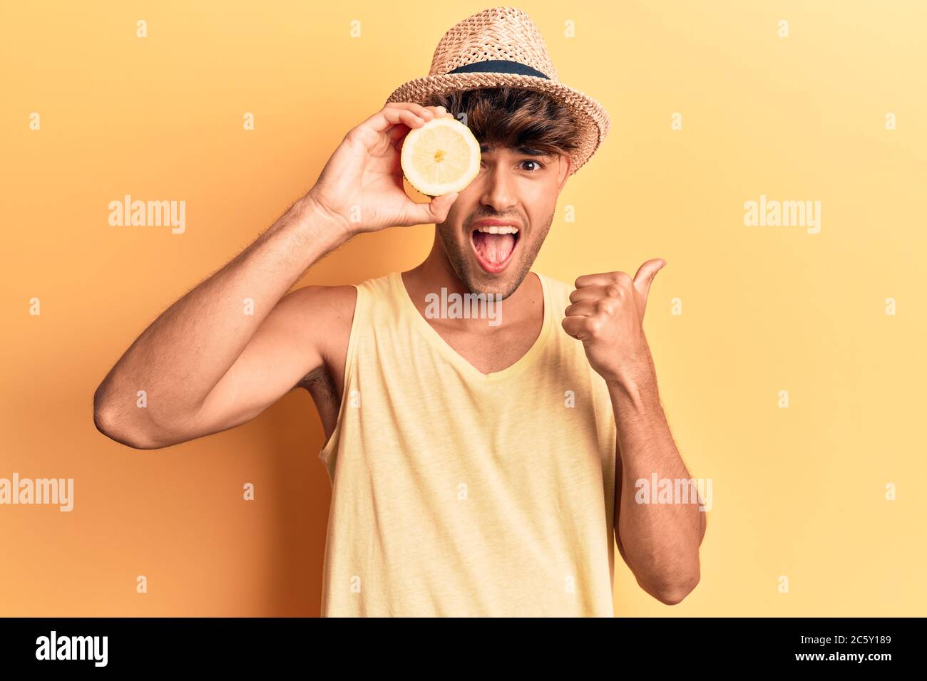 Young hispanic man holding lemon pointing thumb up to the side smiling ...