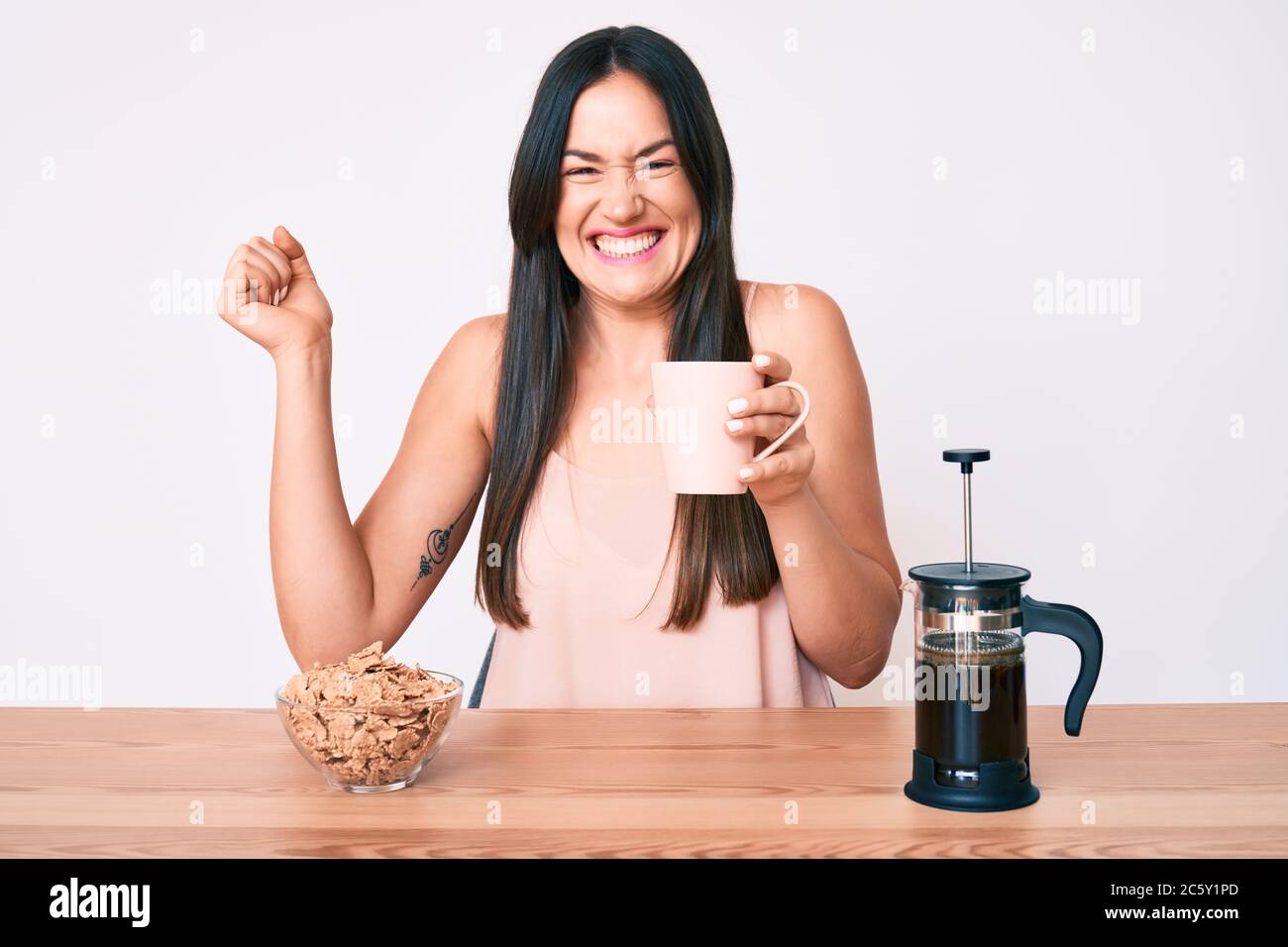 Young caucasian woman sitting at the table drinking coffee screaming ...
