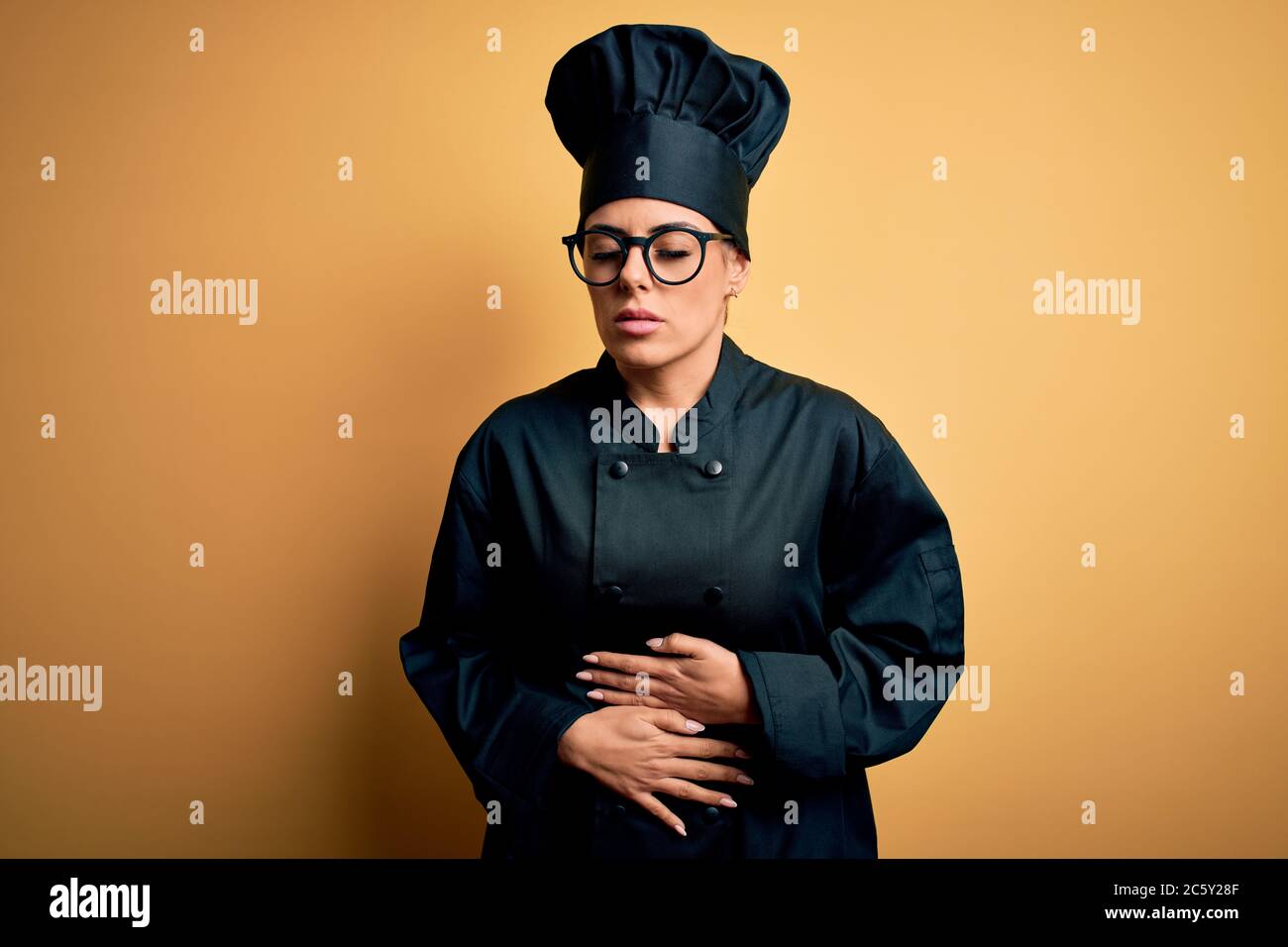 Young beautiful brunette chef woman wearing cooker uniform and hat over ...