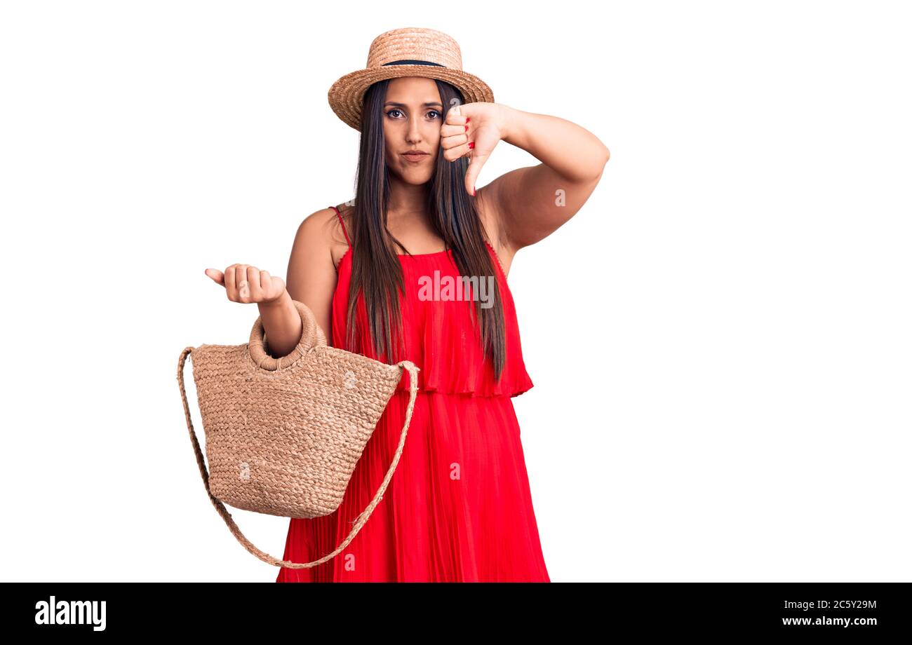 Young beautiful brunette woman wearing summer hat and dress holding bag ...