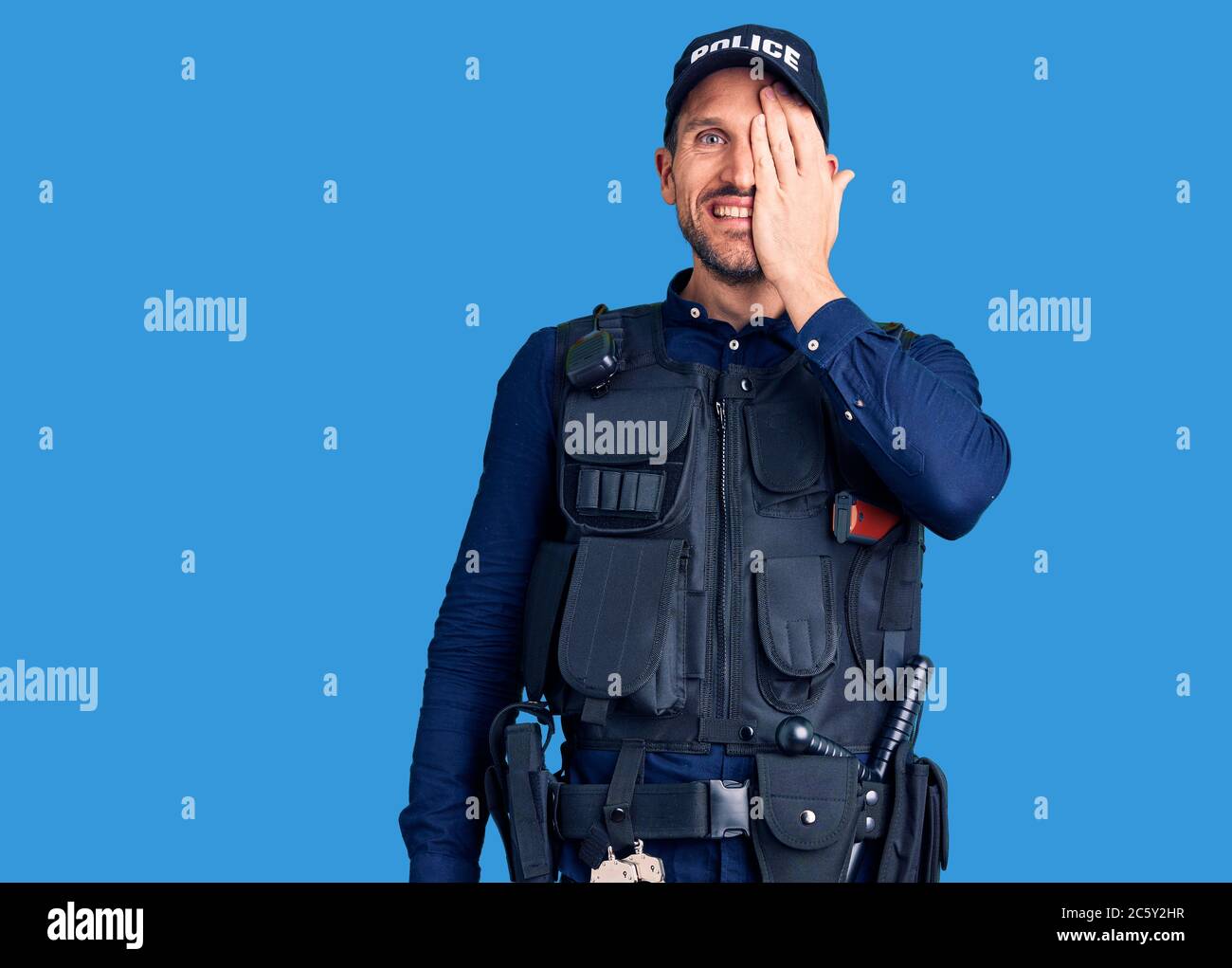Young handsome man wearing police uniform covering one eye with hand ...