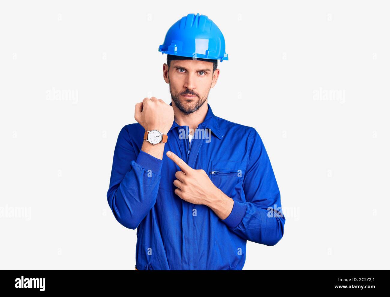 Young handsome man wearing worker uniform and hardhat checking the time ...