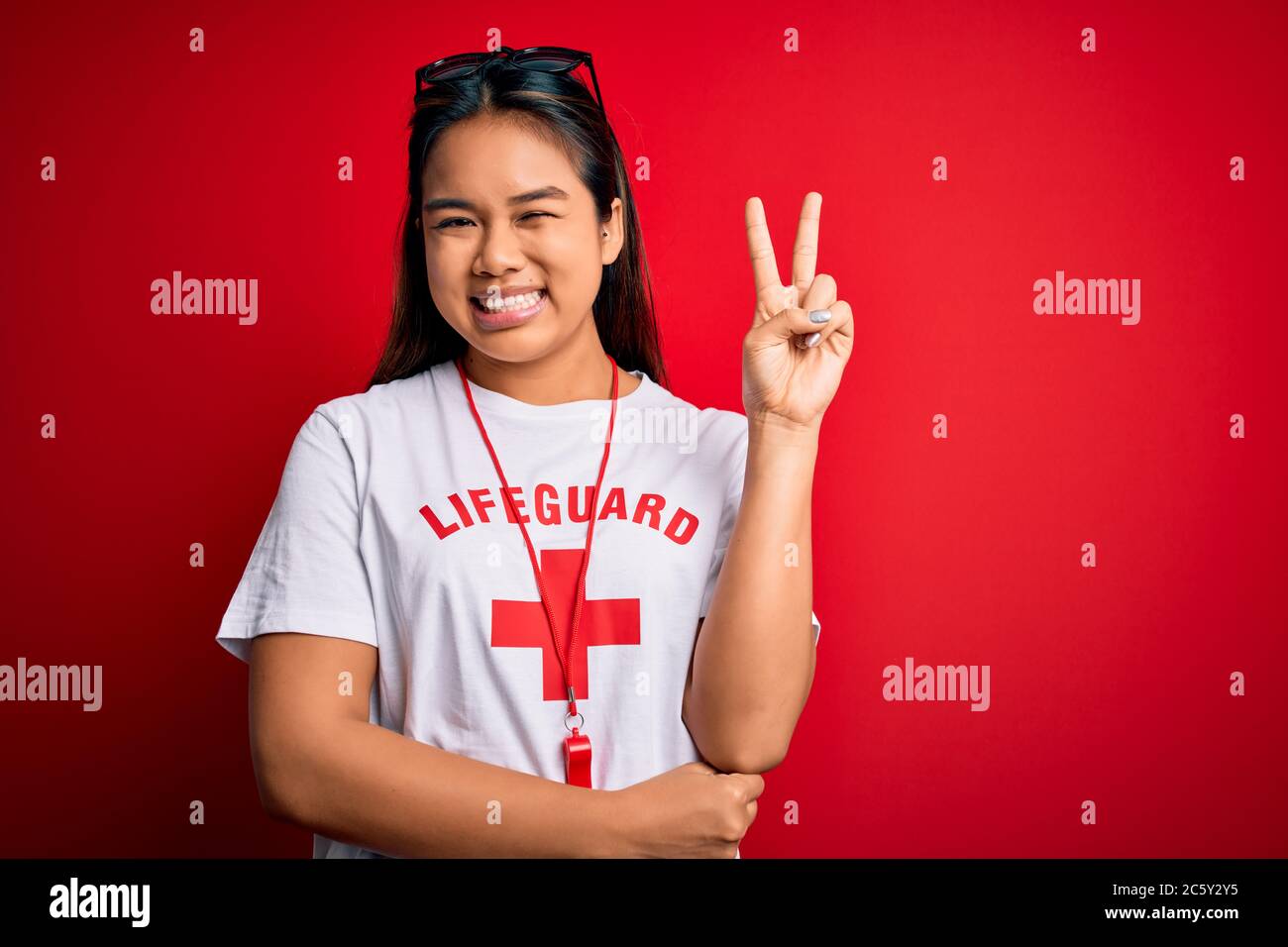 Young asian lifeguard girl wearing t-shirt with red cross using whistle ...