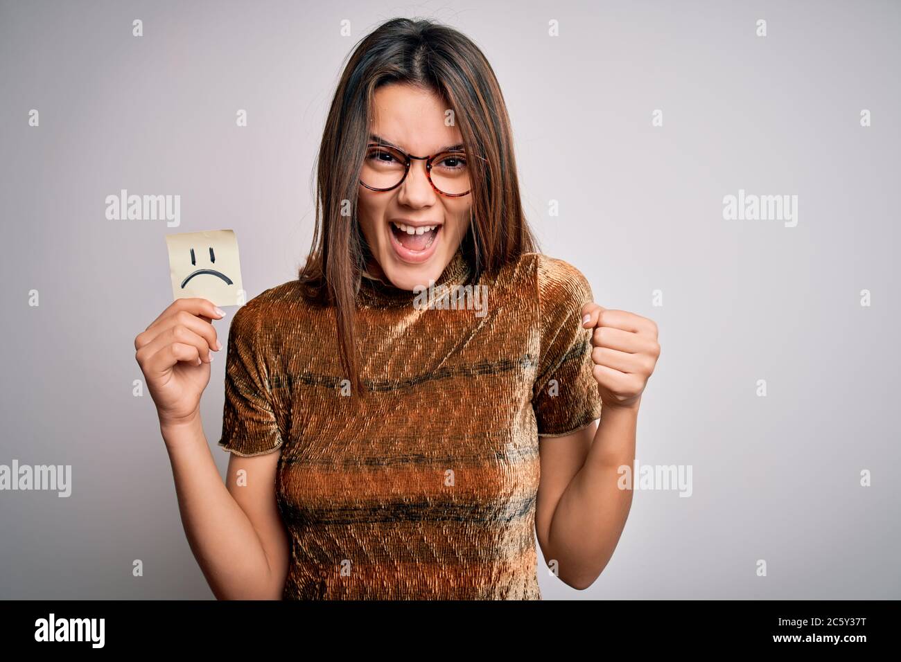 Young beautiful girl holding reminder with sad emotion emoji face over ...