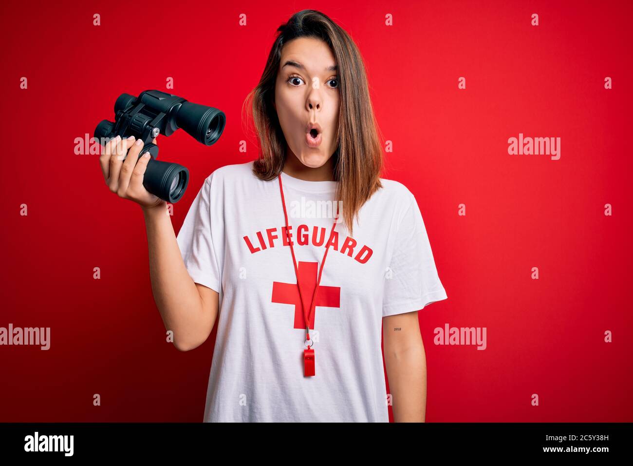 Young beautiful lifeguard girl wearing whistle using binoculars over ...