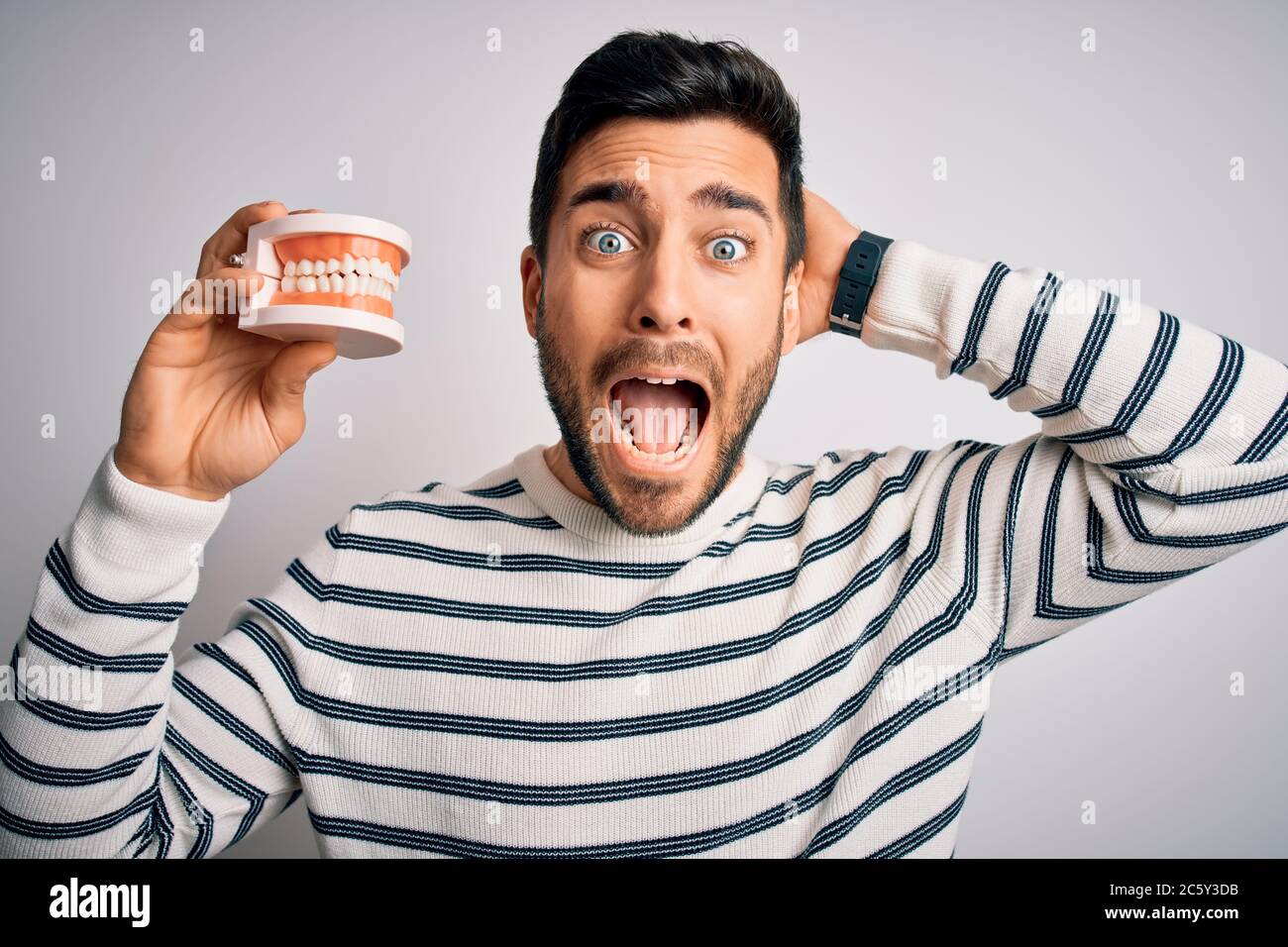 Young handsome man with beard holding plastic denture teeth over white ...