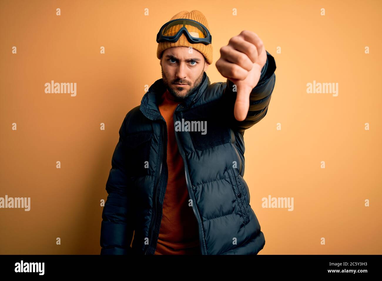 Young handsome skier man with beard wearing snow sportswear and ski ...