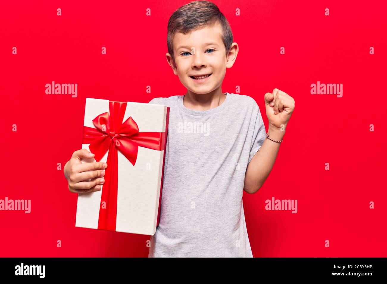 Cute blond kid holding gift screaming proud, celebrating victory and ...