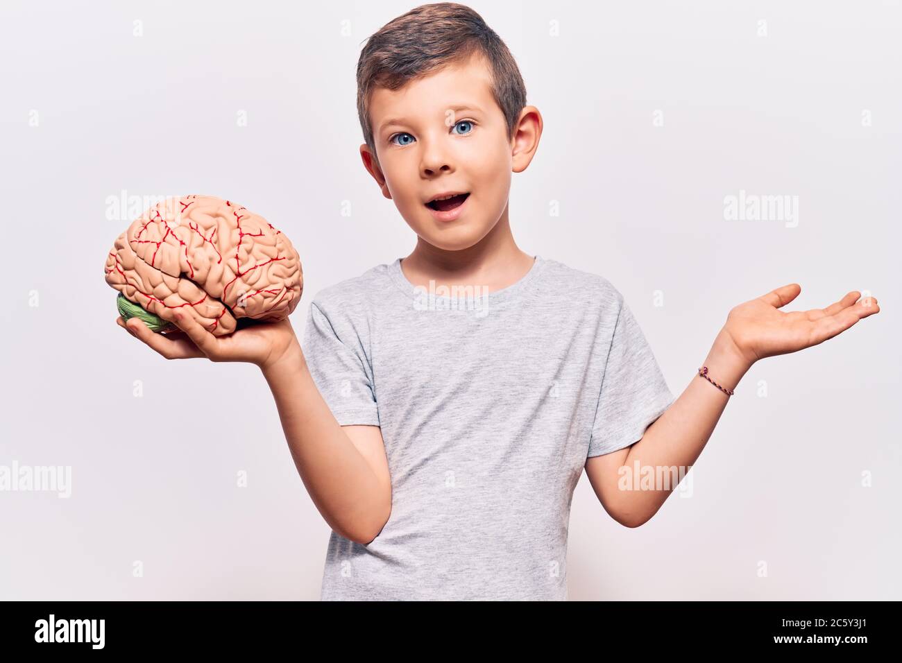 Cute blond kid holding brain celebrating achievement with happy smile ...