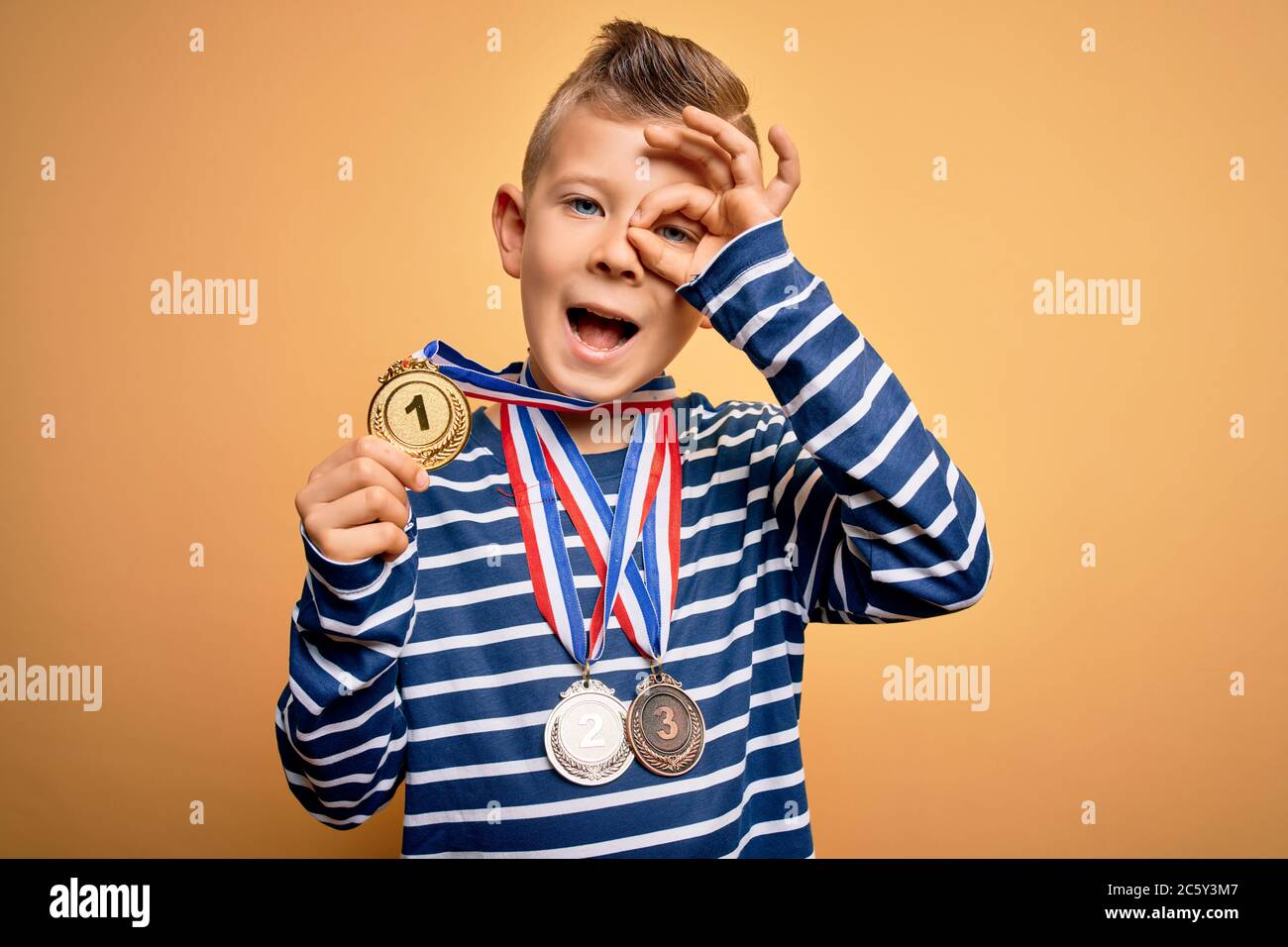 Young little caucasian winner kid wearing award competition medals over ...