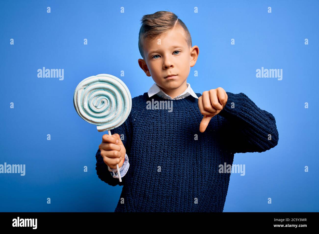 Young little caucasian kid eating sweet candy lollipop over blue ...