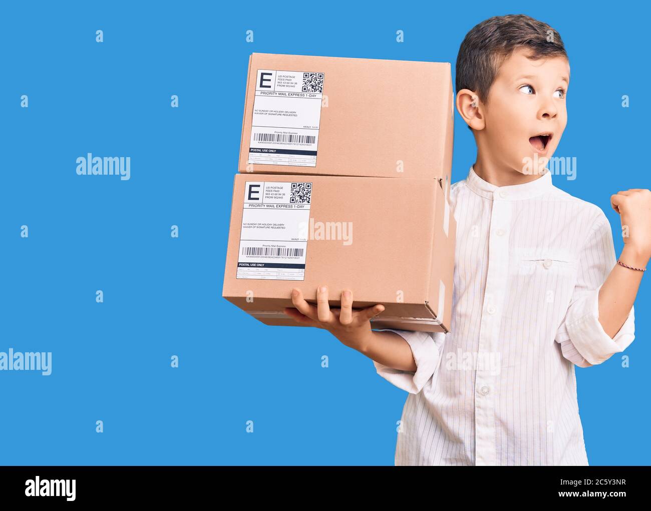 Cute blond kid holding delivery package pointing thumb up to the side ...
