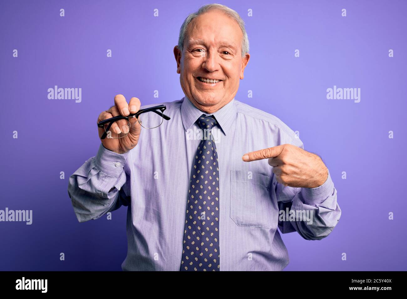 Senior grey haired man holding correction glasses over purple ...