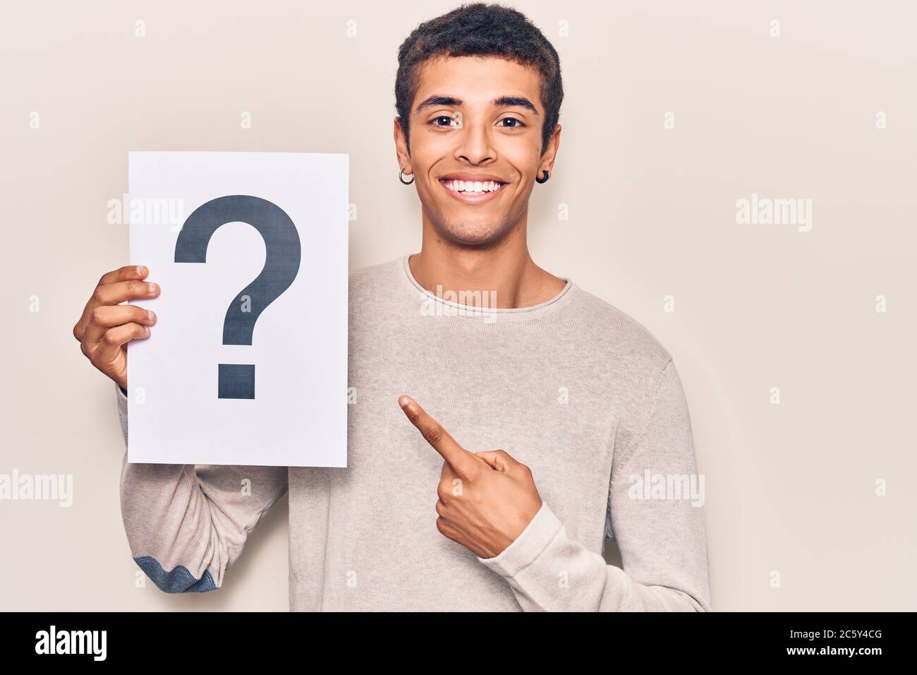 Young african amercian man holding question mark smiling happy pointing ...