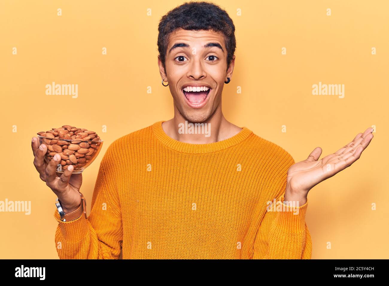 Young african amercian man holding bowl with almonds celebrating ...