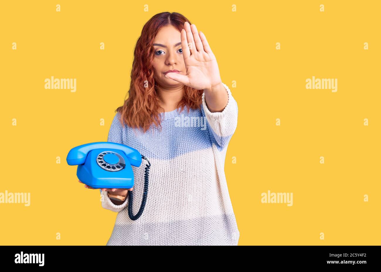 Young latin woman holding vintage telephone with open hand doing stop ...