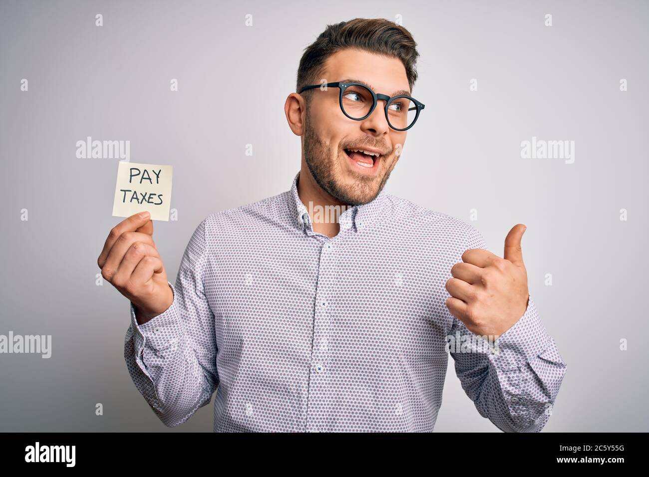 Young business man with blue eyes holding pay taxes word on paper note ...