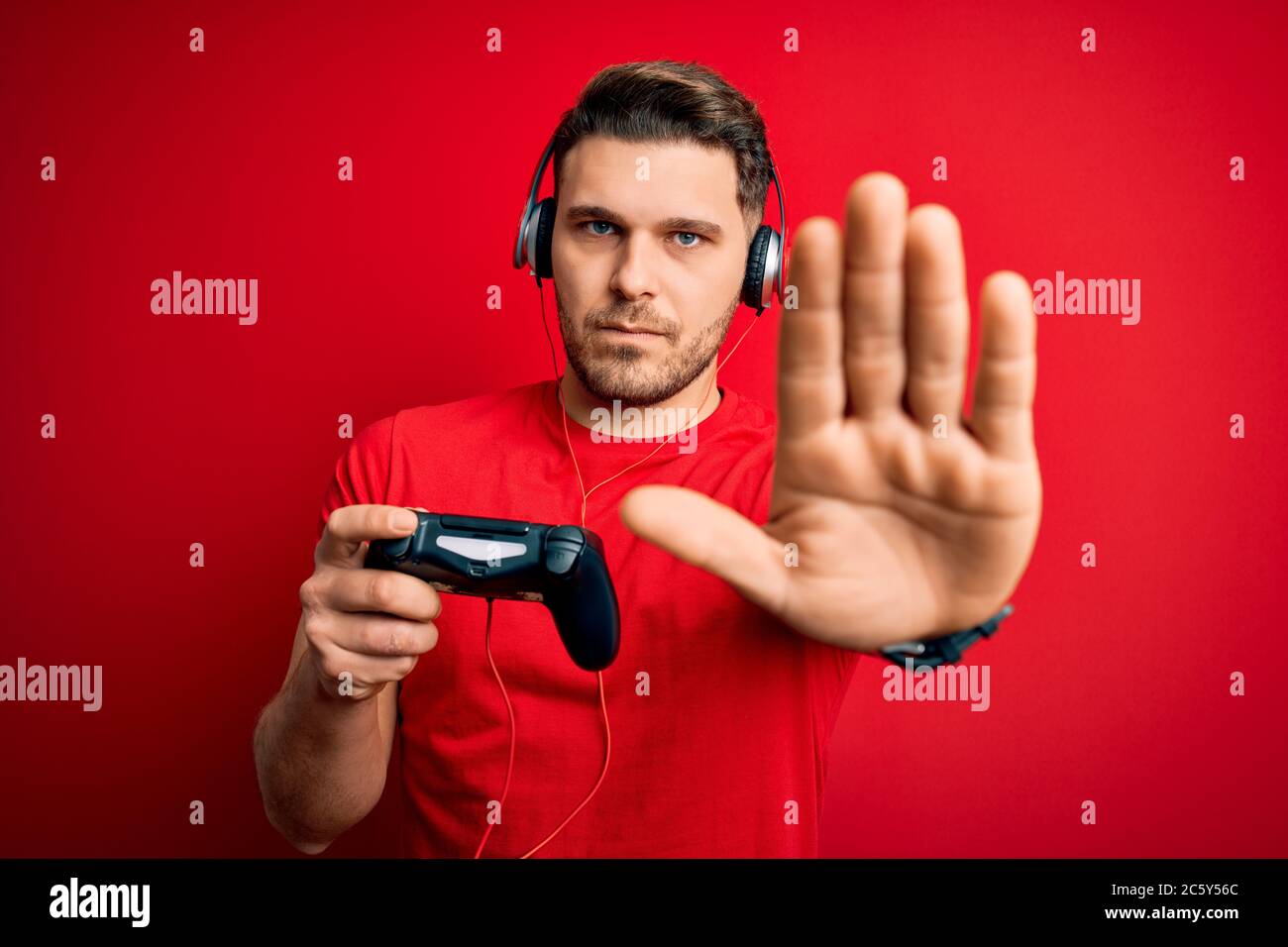 Young gamer man with blue eyes playing video games using gamepad ...
