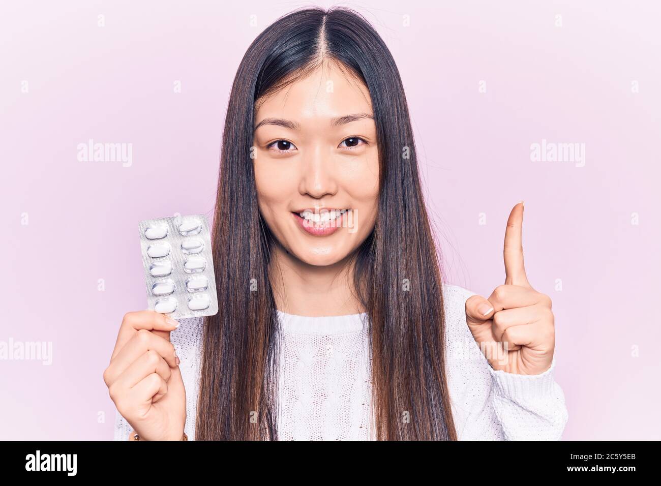 Young beautiful chinese woman holding pills smiling with an idea or ...
