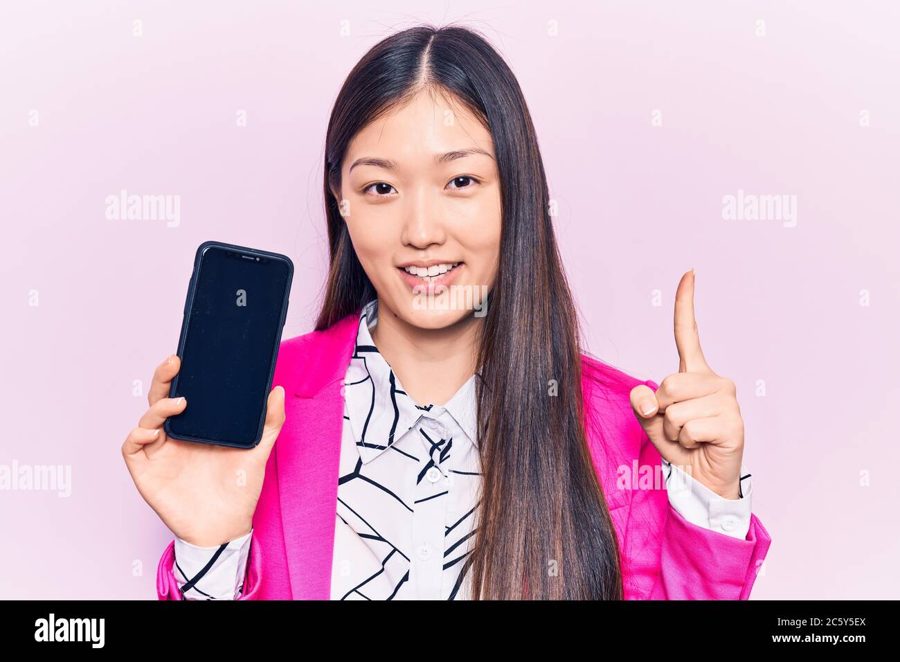Young beautiful chinese woman holding smartphone showing screen smiling ...