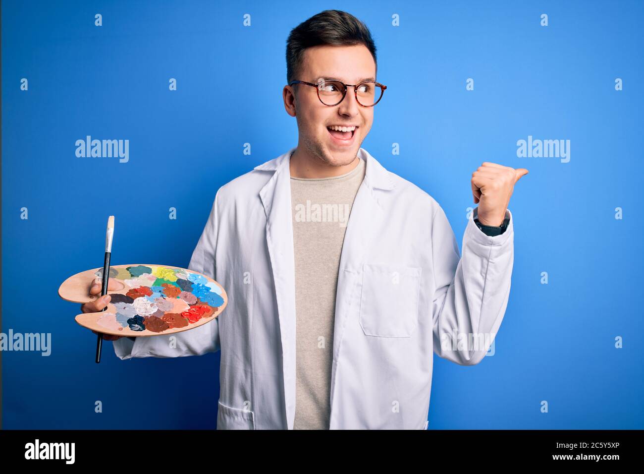Young handsome caucasian artist man holding paintbrush and painter ...