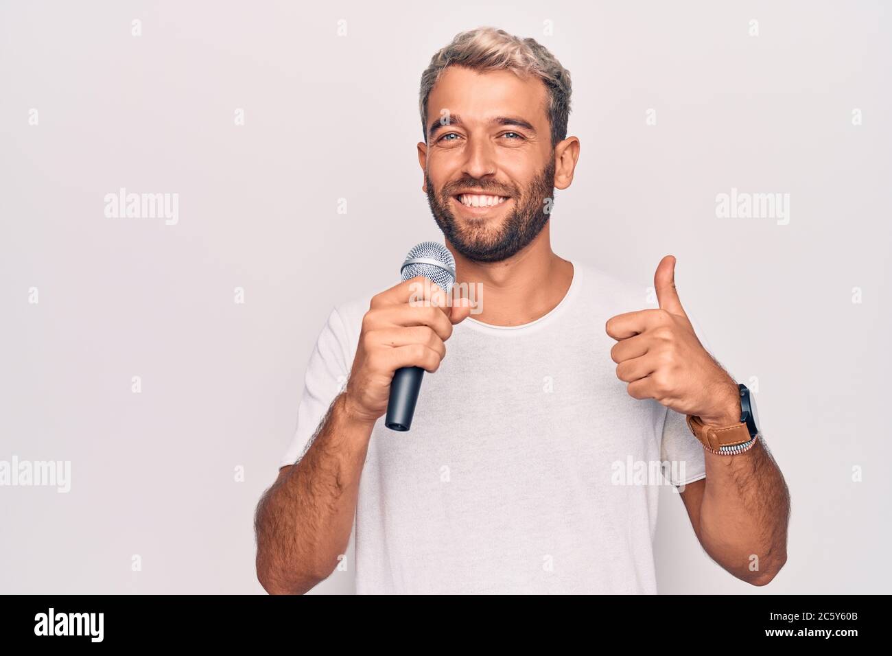 Handsome blond singer man with beard singing song using microphone over white background smiling ...