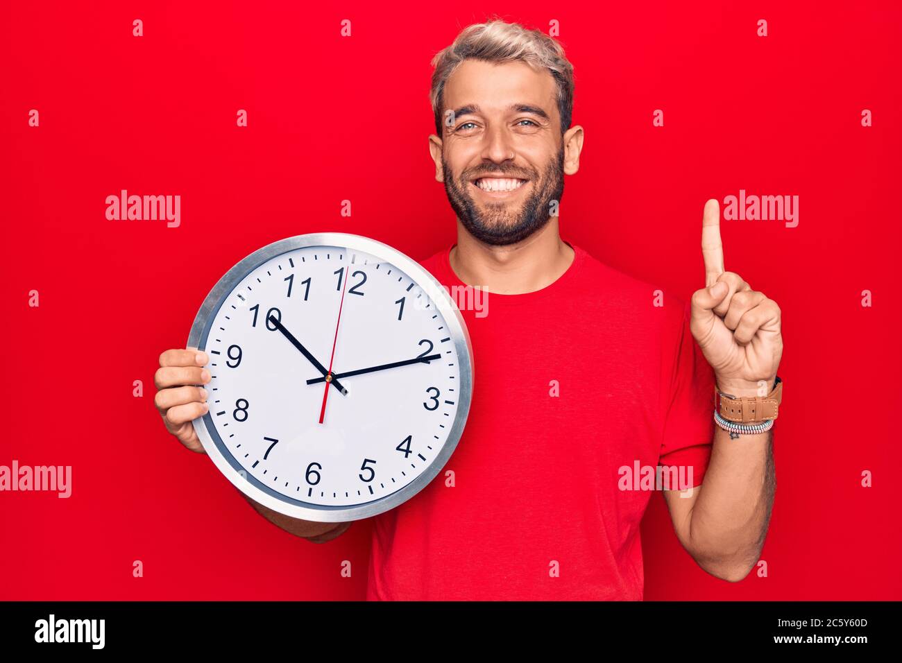 Young handsome blond man with beard doing countdown using big clock ...