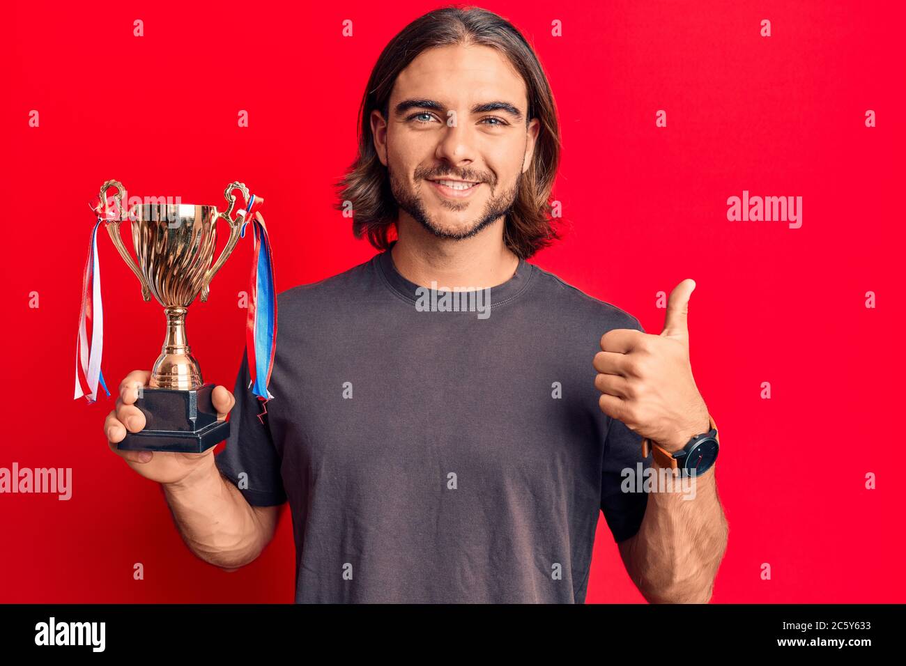 Young handsome man holding winner trophy smiling happy and positive ...