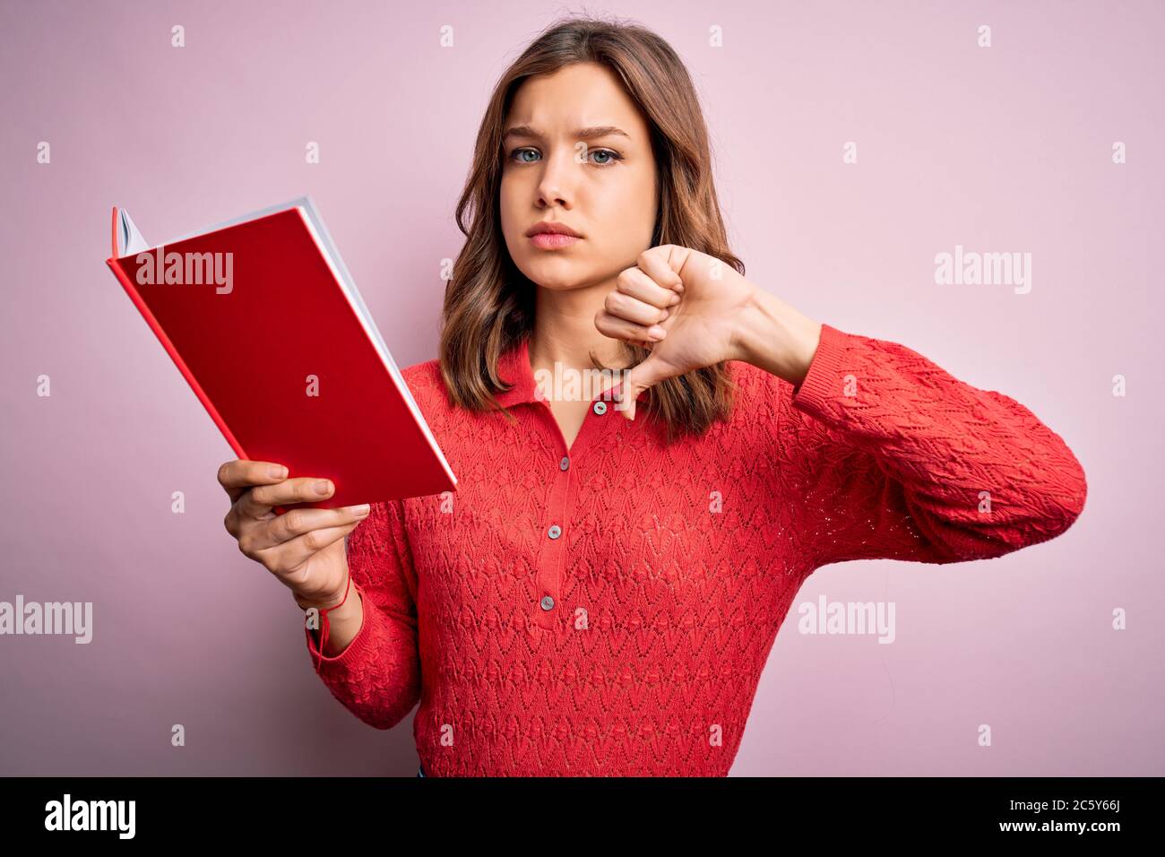Young blonde student girl reading a book over pink isolated background ...