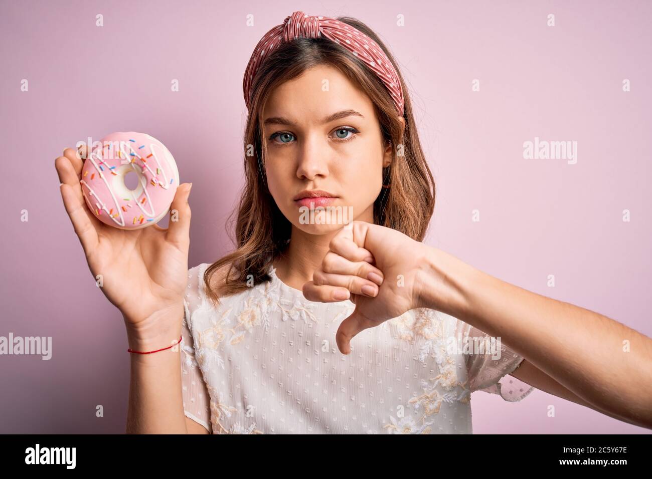 Young blonde girl eating sweet bakery sugar doughnut over pink isolated ...