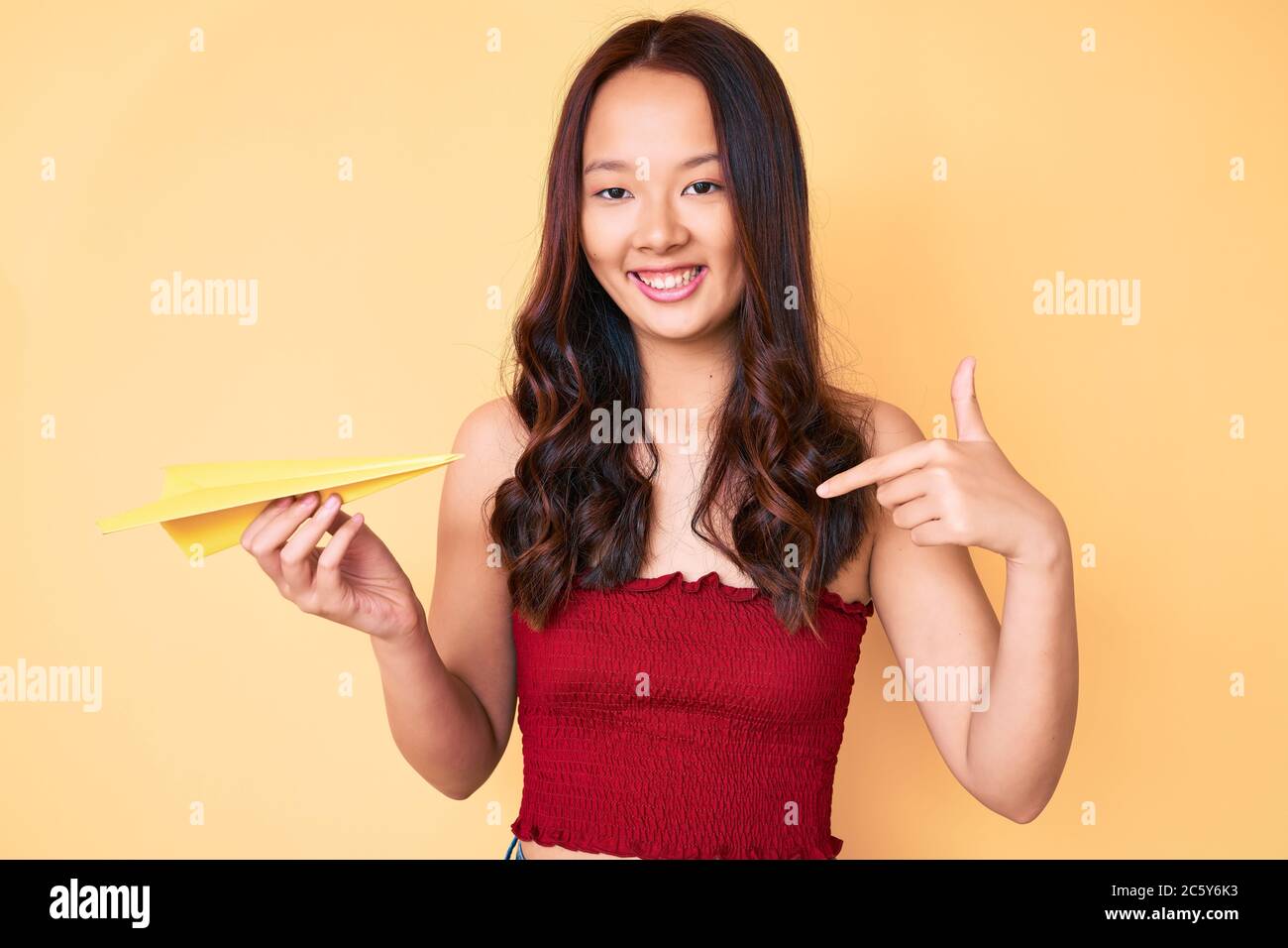 Young beautiful chinese girl holding paper airplane pointing finger to ...