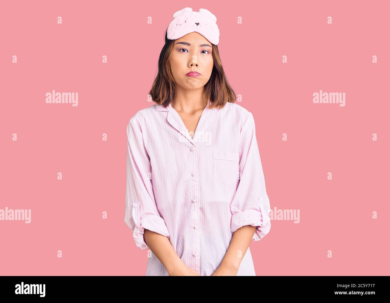 Young beautiful chinese girl wearing sleep mask and pajama depressed ...